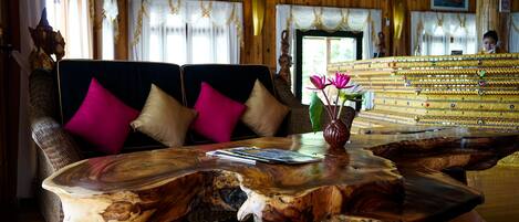 Interior em madeira com uma grande mesa de centro, assentos acolchoados e um vaso decorativo.