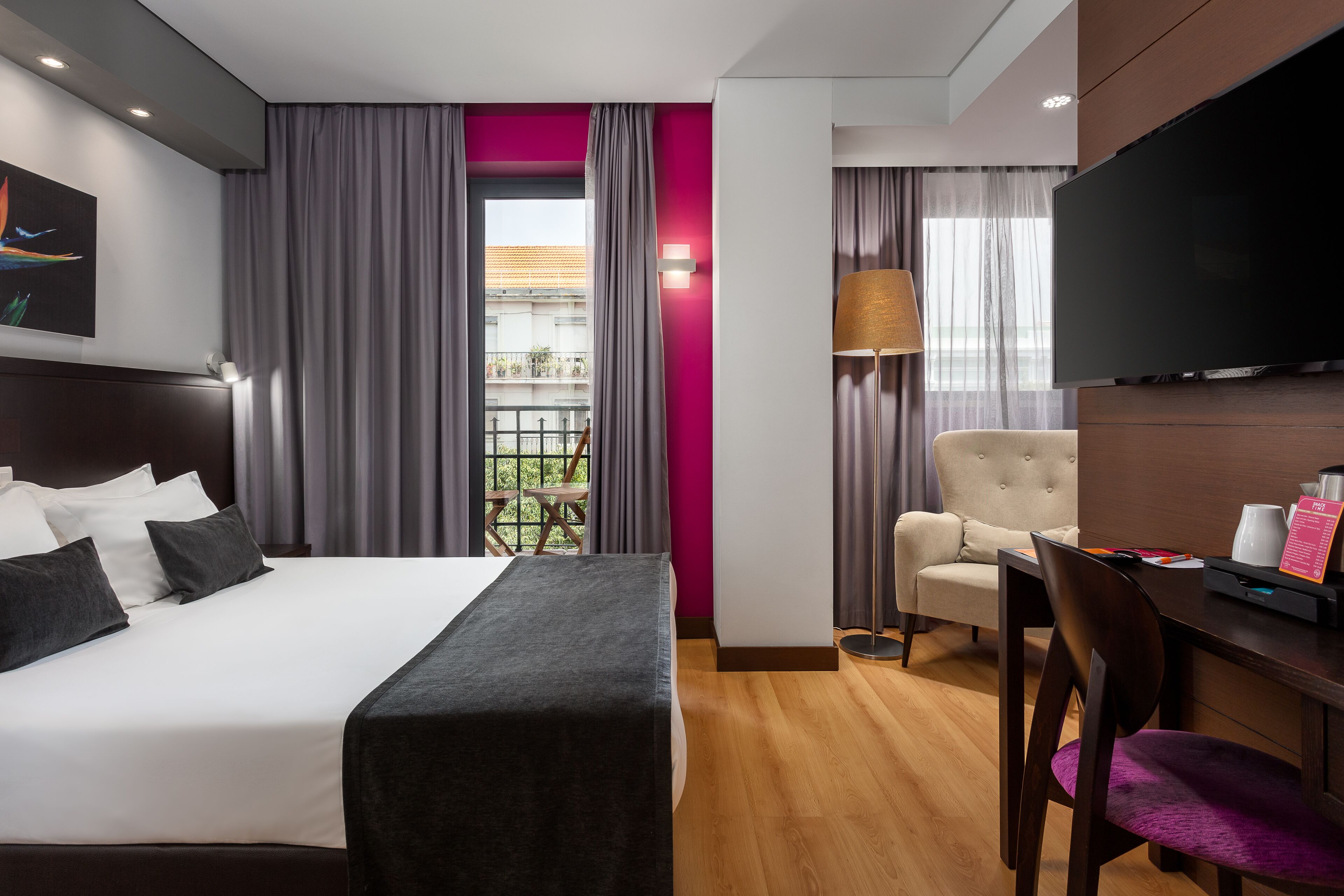 Quarto de hotel com uma cama, uma escrivaninha com cadeira, televisão e janela com cortinas.