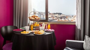 Mesa de café da manhã com doces, frutas e bebidas, com vista para a cidade.