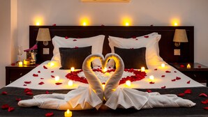 Cama com pétalas de rosa e velas, duas almofadas e arranjo de toalhas em formato de coração.