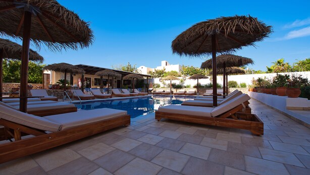 Uma área de piscina com espreguiçadeiras e guarda-sóis de palha.