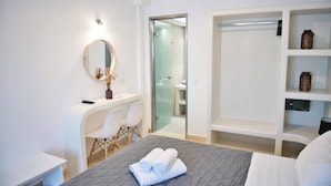Quarto de hotel com cama, escrivaninha com cadeira, guarda-roupa e banheiro visível por uma porta aberta.