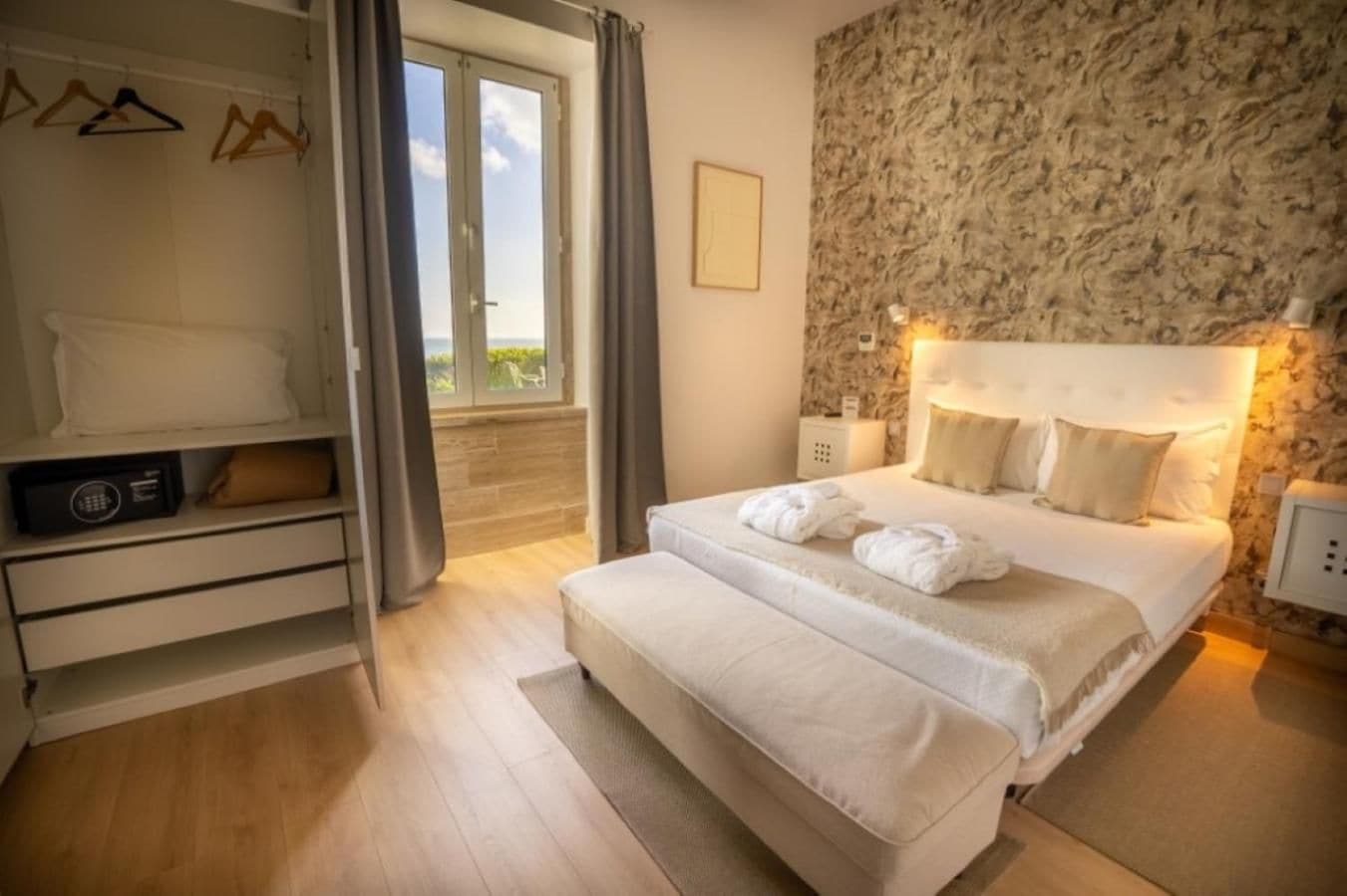 Quarto com cama, mesa de cabeceira, armário e vista para o exterior.