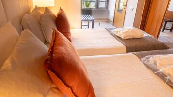 Quarto de hotel com duas camas, uma mesinha e janela com vista.