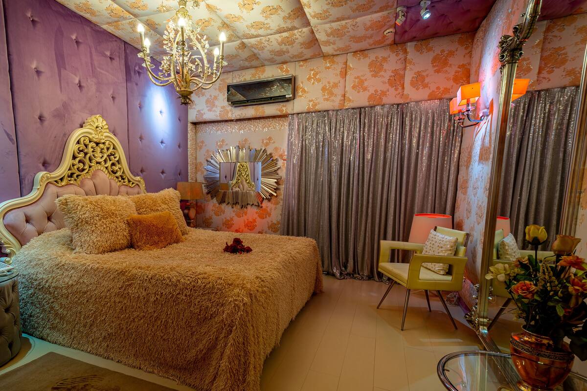 Quarto com cabeceira estofada, um espelho grande, um candelabro e uma cama com roupa de cama fofa.