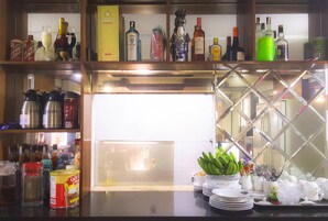 Uma área de bar com prateleiras de garrafas, uma máquina de café e uma exposição de bananas e pratos.