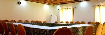 Sala de conferência com uma mesa comprida cercada por cadeiras, um quadro branco e uma janela com cortinas.