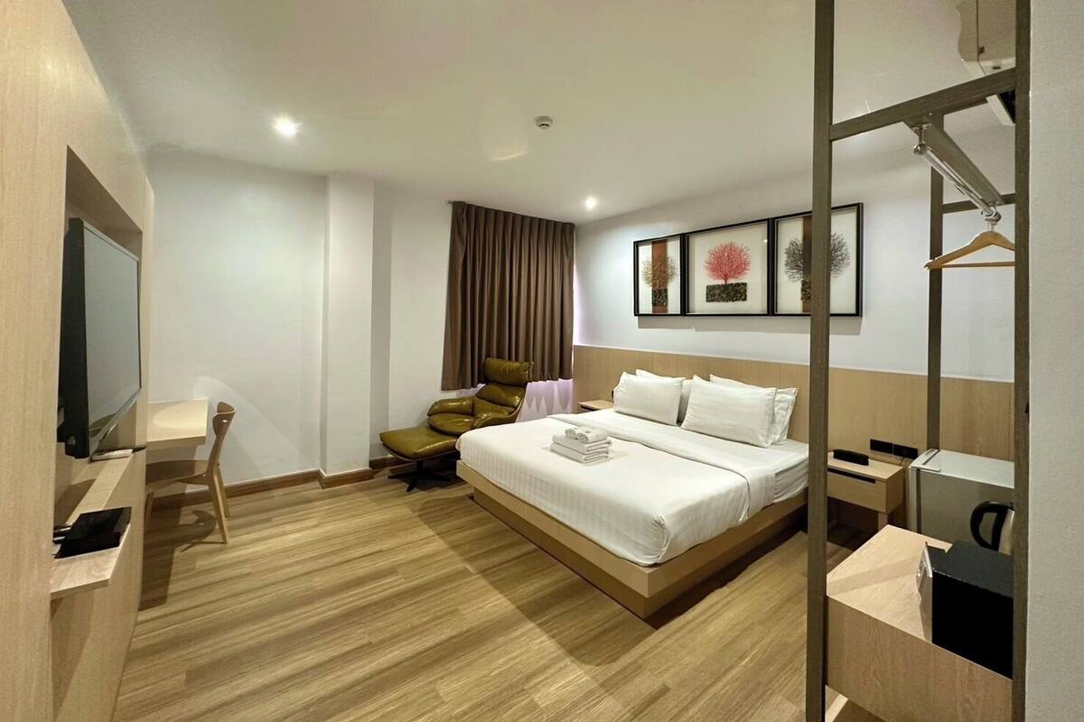 Quarto de hotel moderno com cama, escrivaninha, cadeira e televisão.