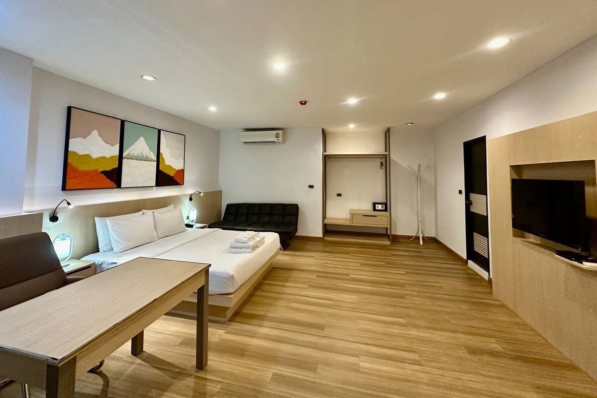 Quarto de hotel moderno com cama, escrivaninha, cadeira, televisão e obras de arte na parede.