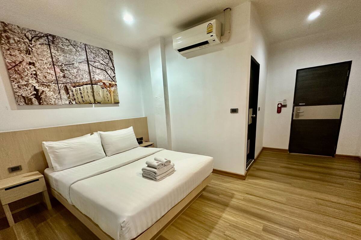 Quarto de hotel com cama, mesa de cabeceira, ar condicionado, porta e uma obra de arte pendurada na parede.