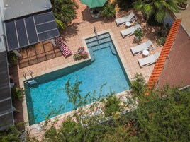 Vista aérea de uma piscina com deck ladrilhado, cadeiras de descanso e plantas em vasos.