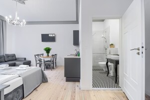 Quarto moderno com sofá, mesa de jantar e pequena área de cozinha.