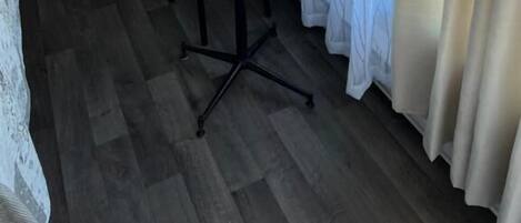 Quarto pequeno com uma mesa redonda e duas cadeiras, uma janela com cortinas leves e parede com padrão.