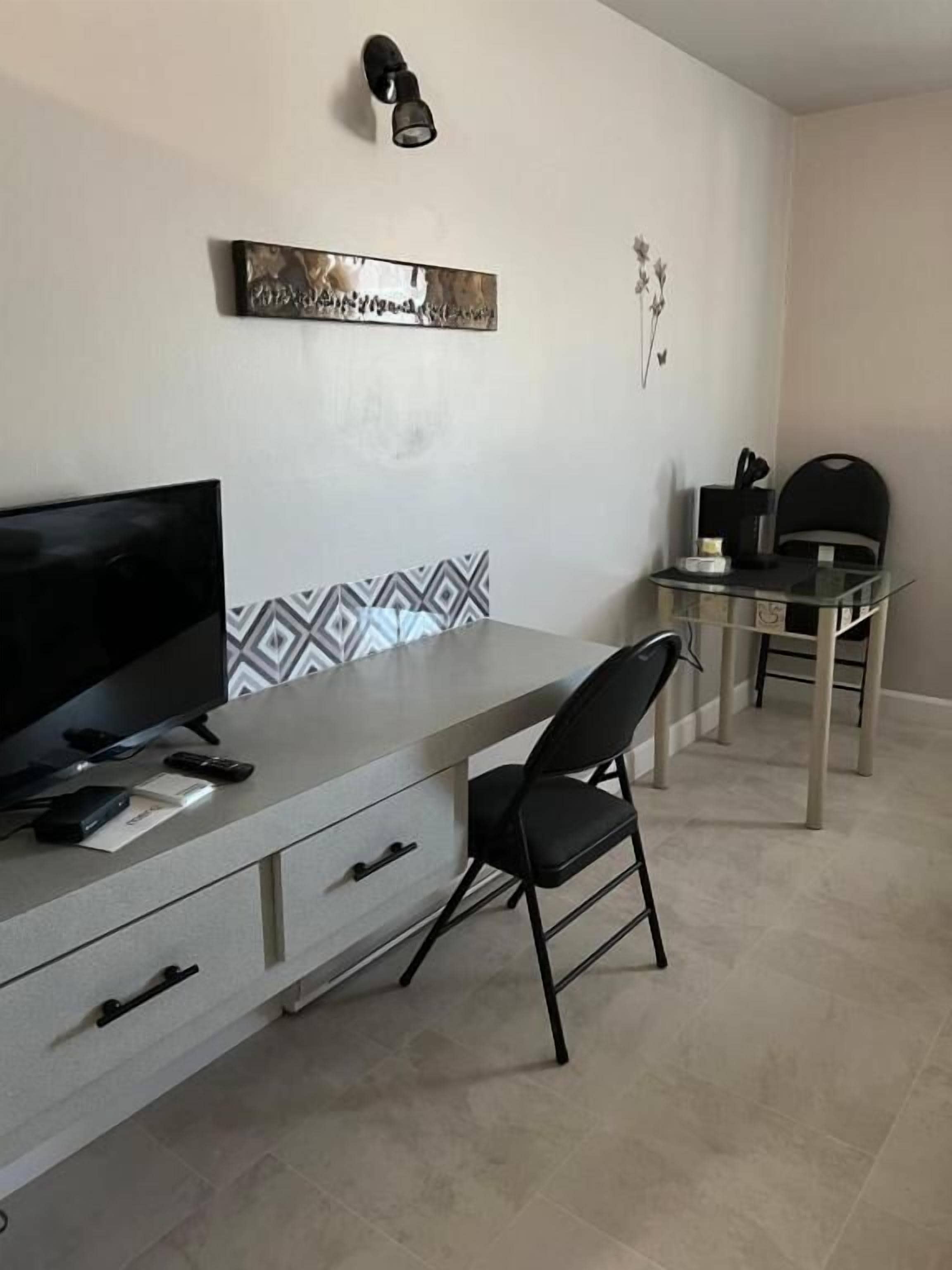 Quarto moderno com TV de tela plana, escrivaninha com cadeira e um detalhe decorativo na parede.