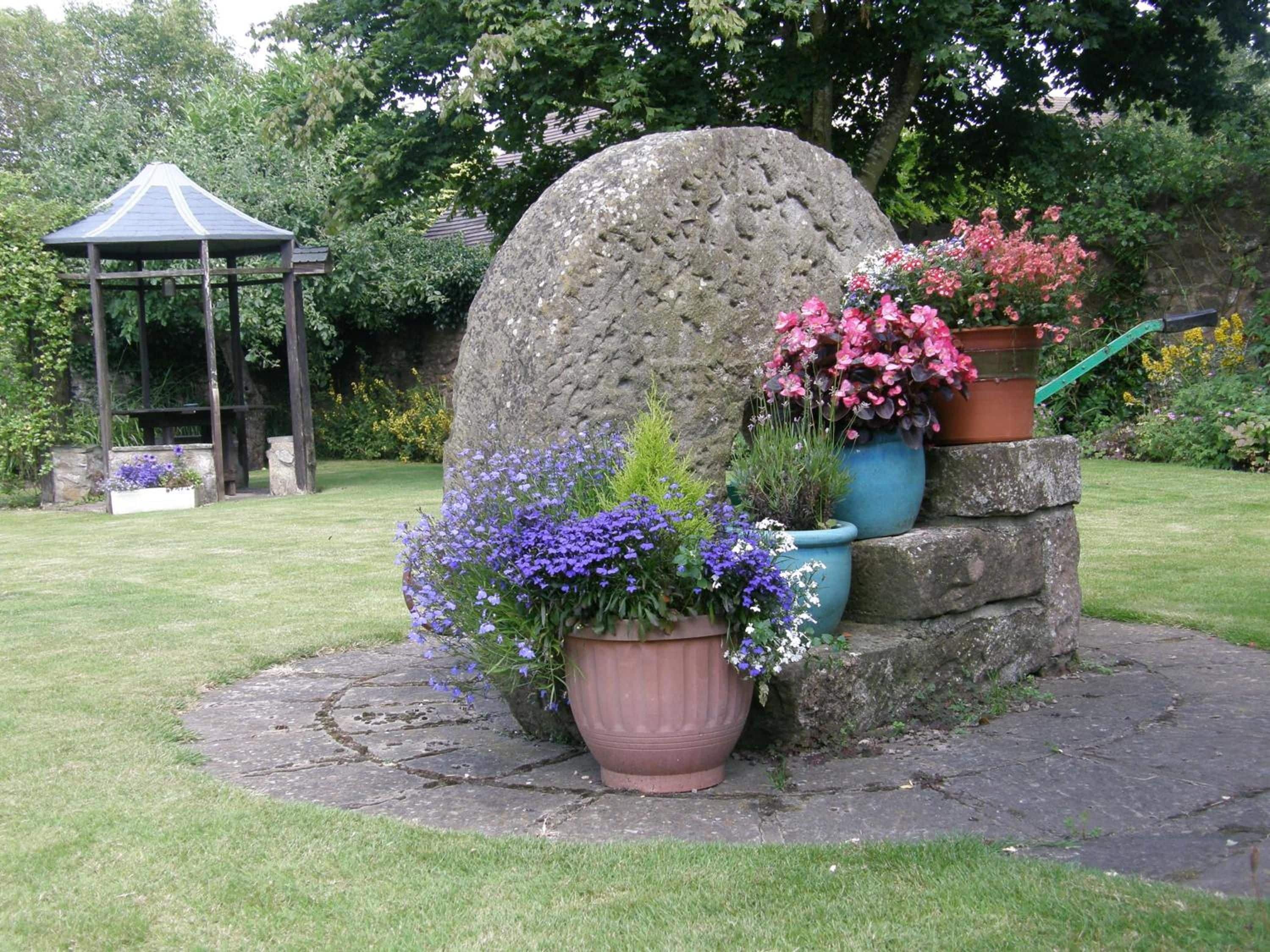 Um jardim com estrutura de pedra, plantas em vasos e um gazebo.