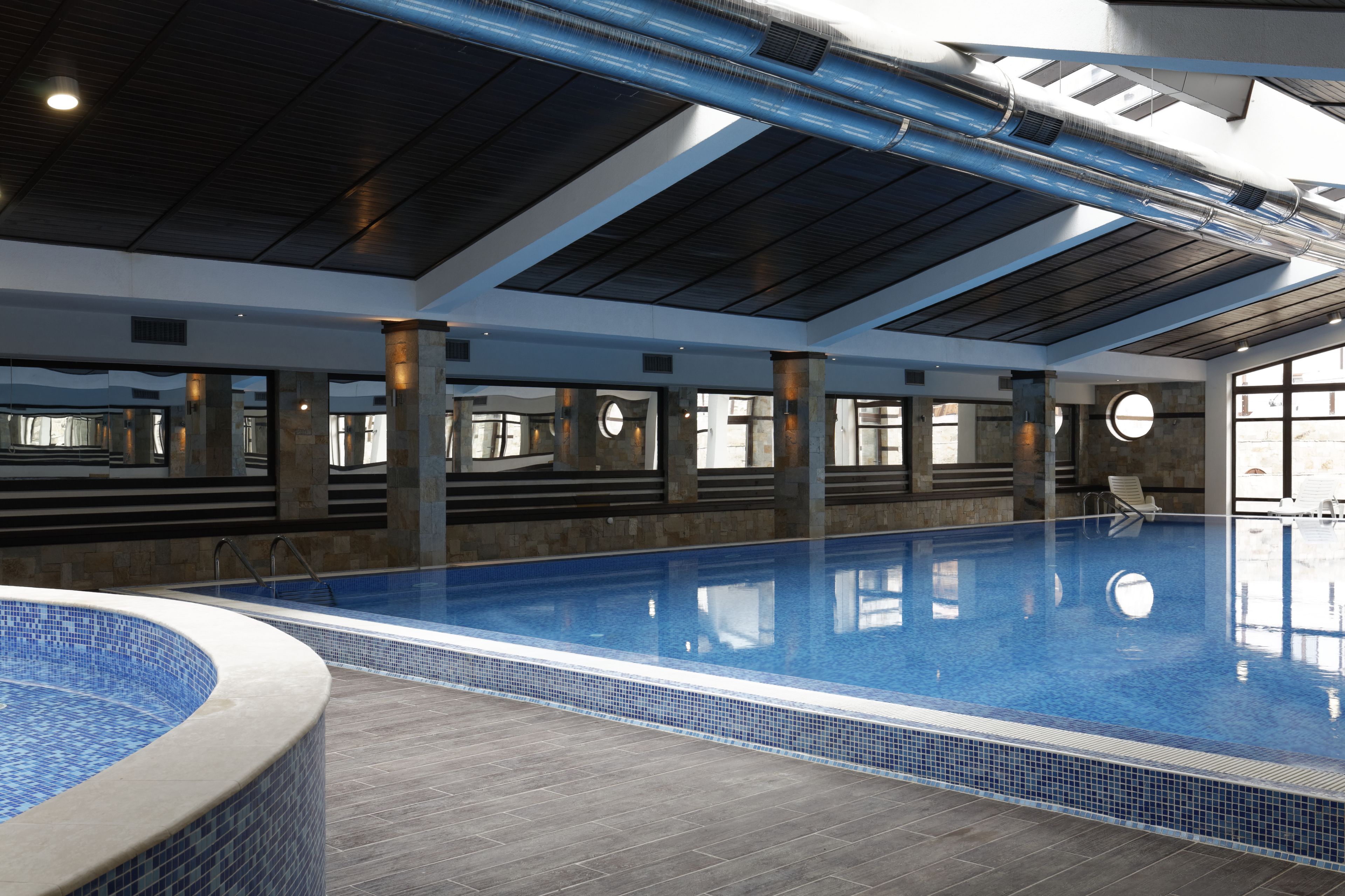 Piscina interna com borda azulejada, área de estar com cadeiras e teto alto com dutos aparentes.