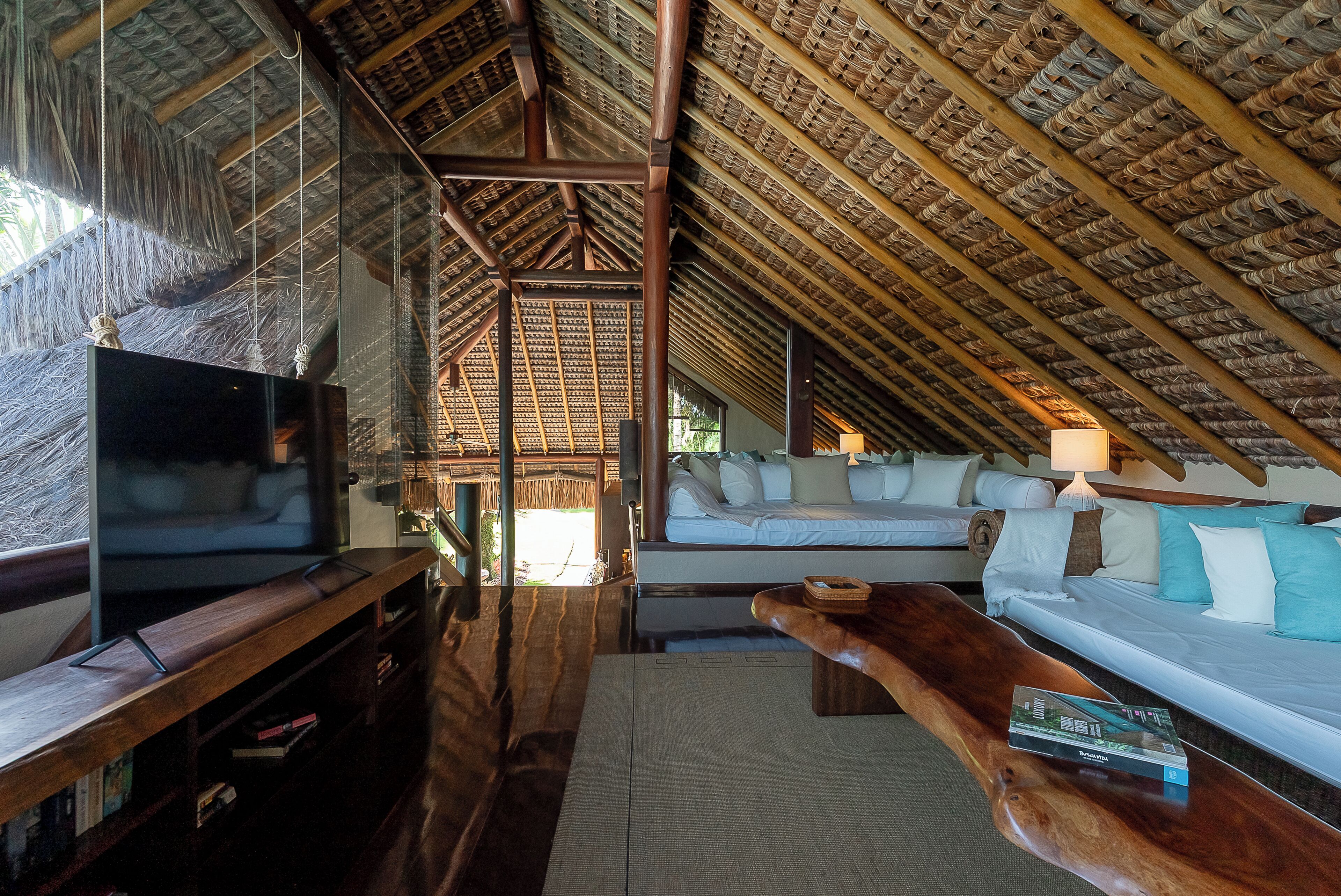 Quarto com televisão, móveis de madeira, sofá e cama com almofadas.