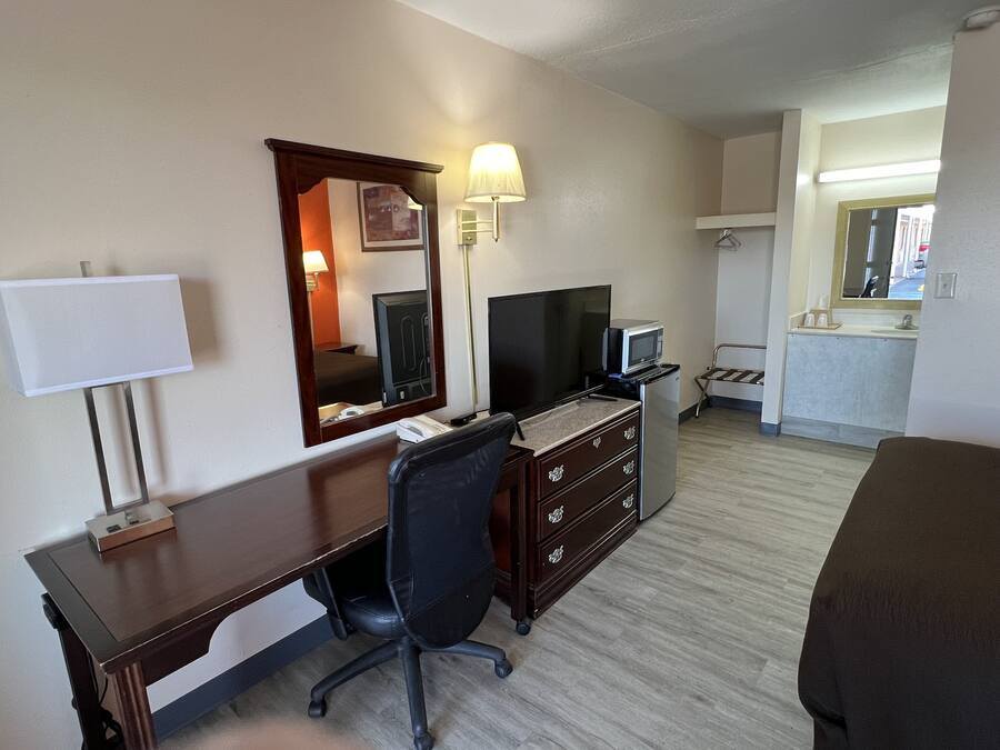 Quarto de hotel com escrivaninha, cadeira, TV, micro-ondas e uma pequena cozinha equipada.