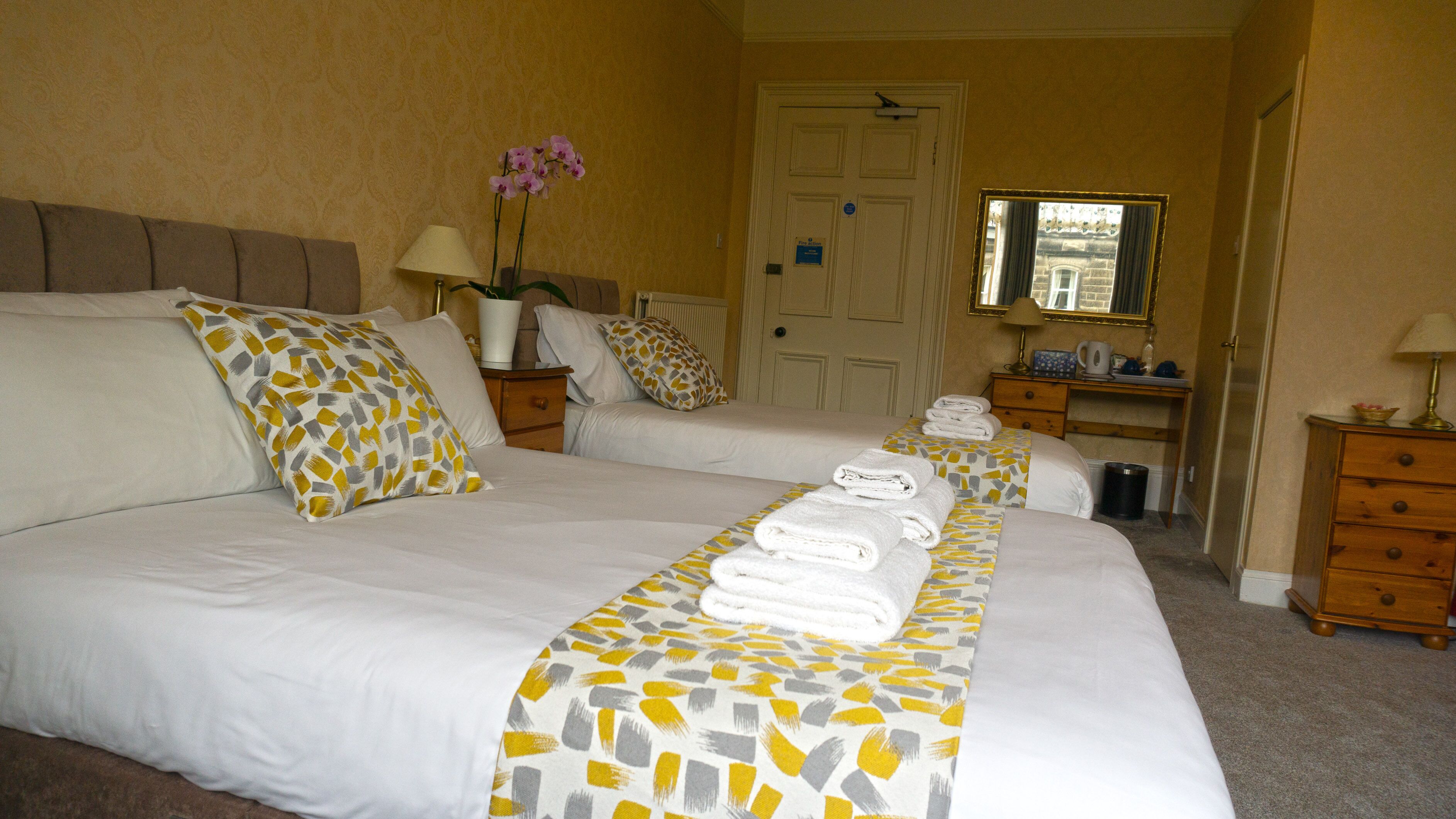 Quarto de hotel com duas camas, uma cômoda, um espelho e uma porta.