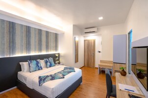 Quarto de hotel moderno com uma cama grande, uma mesa de trabalho com cadeira, um espelho e piso de madeira.
