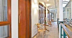 Um corredor com portas de madeira, cadeiras de vime e um corrimão.