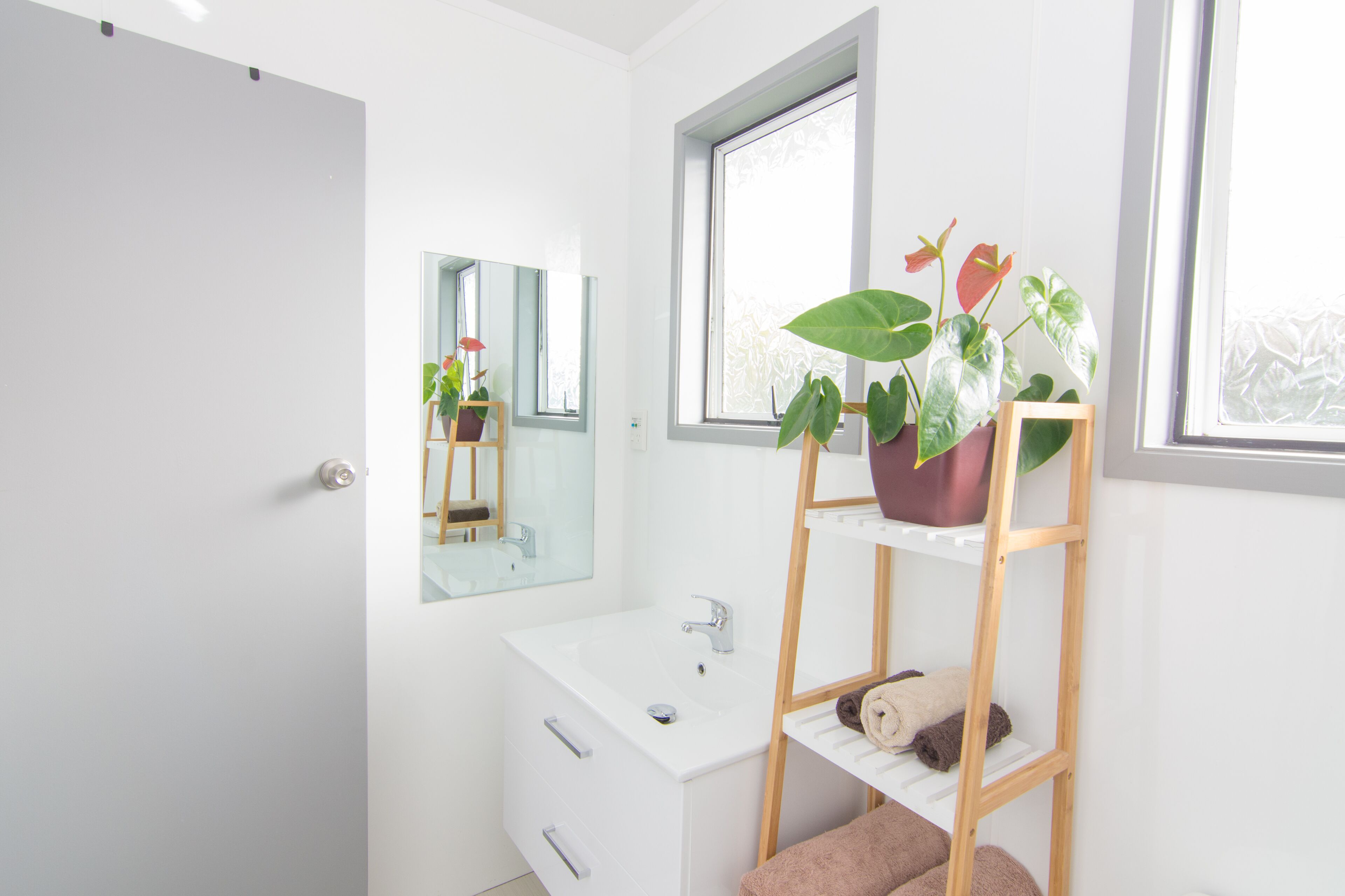 Uma casa de banho moderna com uma sanita branca, espelho e uma prateleira de madeira com uma planta e toalhas.