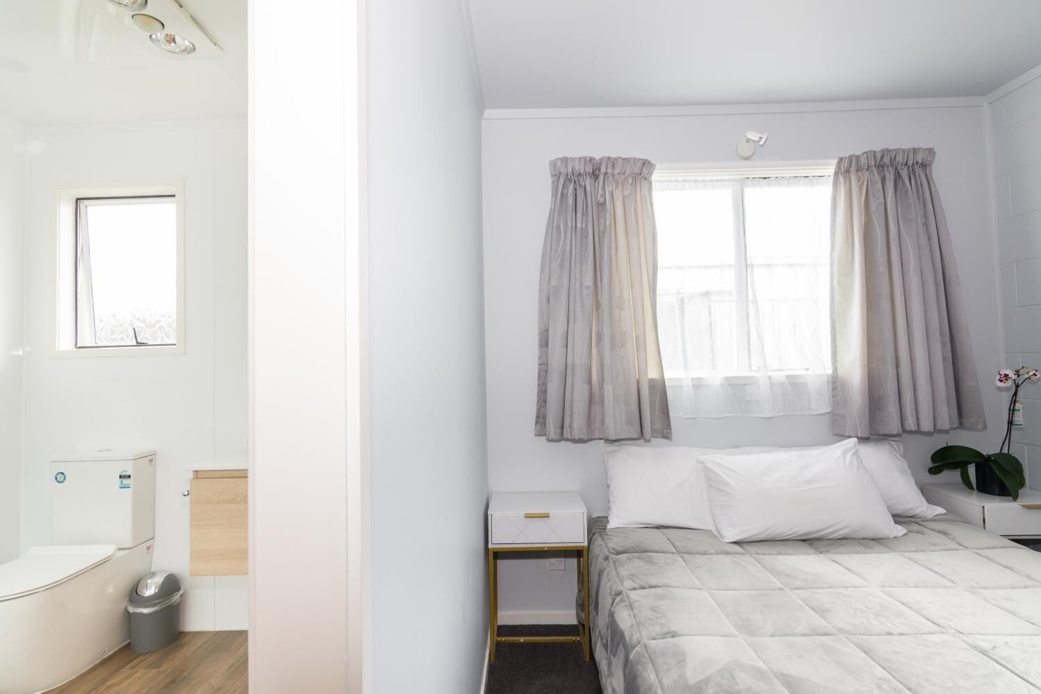Quarto com cama, mesa de cabeceira e janela com cortinas.