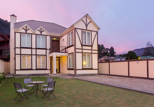 Uma casa de dois andares com varanda, um pequeno pátio com mesa e cadeiras, e um gramado bem cuidado.