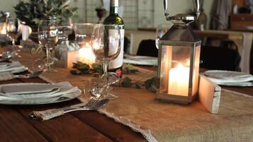 Mesa de jantar posta com taças de vinho, pratos, talheres e uma vela acesa em ambiente rústico.