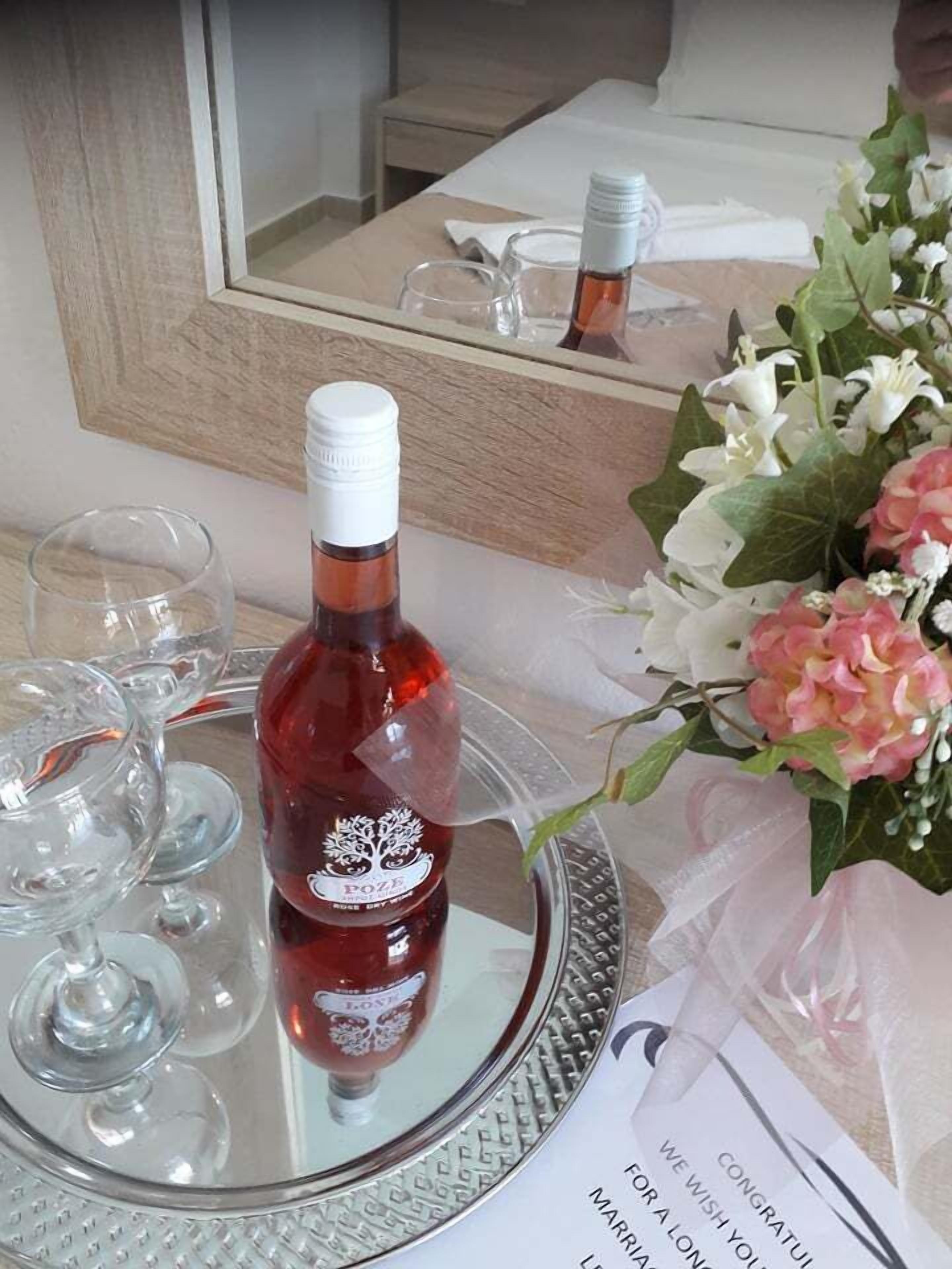 Uma garrafa de vinho rosé em um tabuleiro com copos, um buquê de flores e um bilhete de congratulações sobre uma mesa.