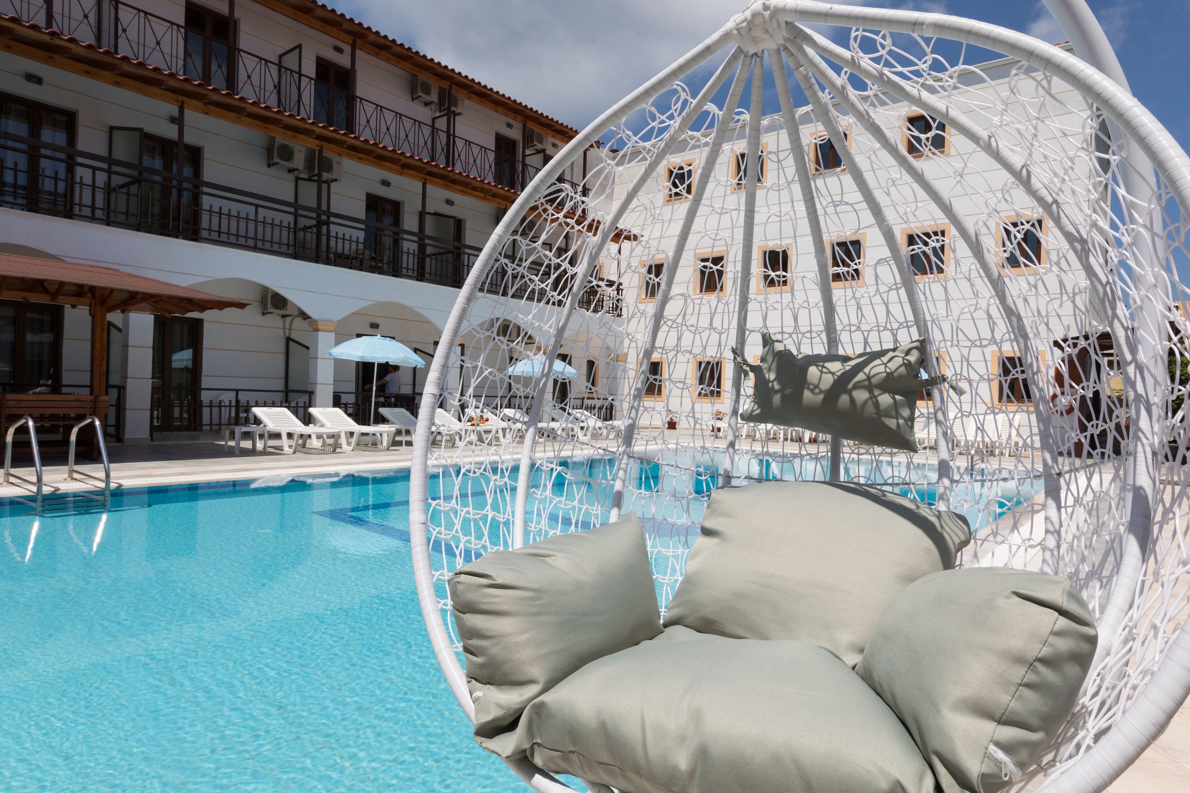 Uma área de piscina com uma cadeira suspensa, espreguiçadeiras e guarda-sóis.