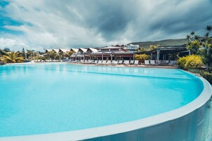Uma piscina grande com espreguiçadeiras e um edifício de resort ao fundo.