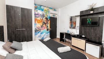 Quarto de hotel moderno com uma cama grande, uma escrivaninha, um frigorífico pequeno e uma televisão na parede.