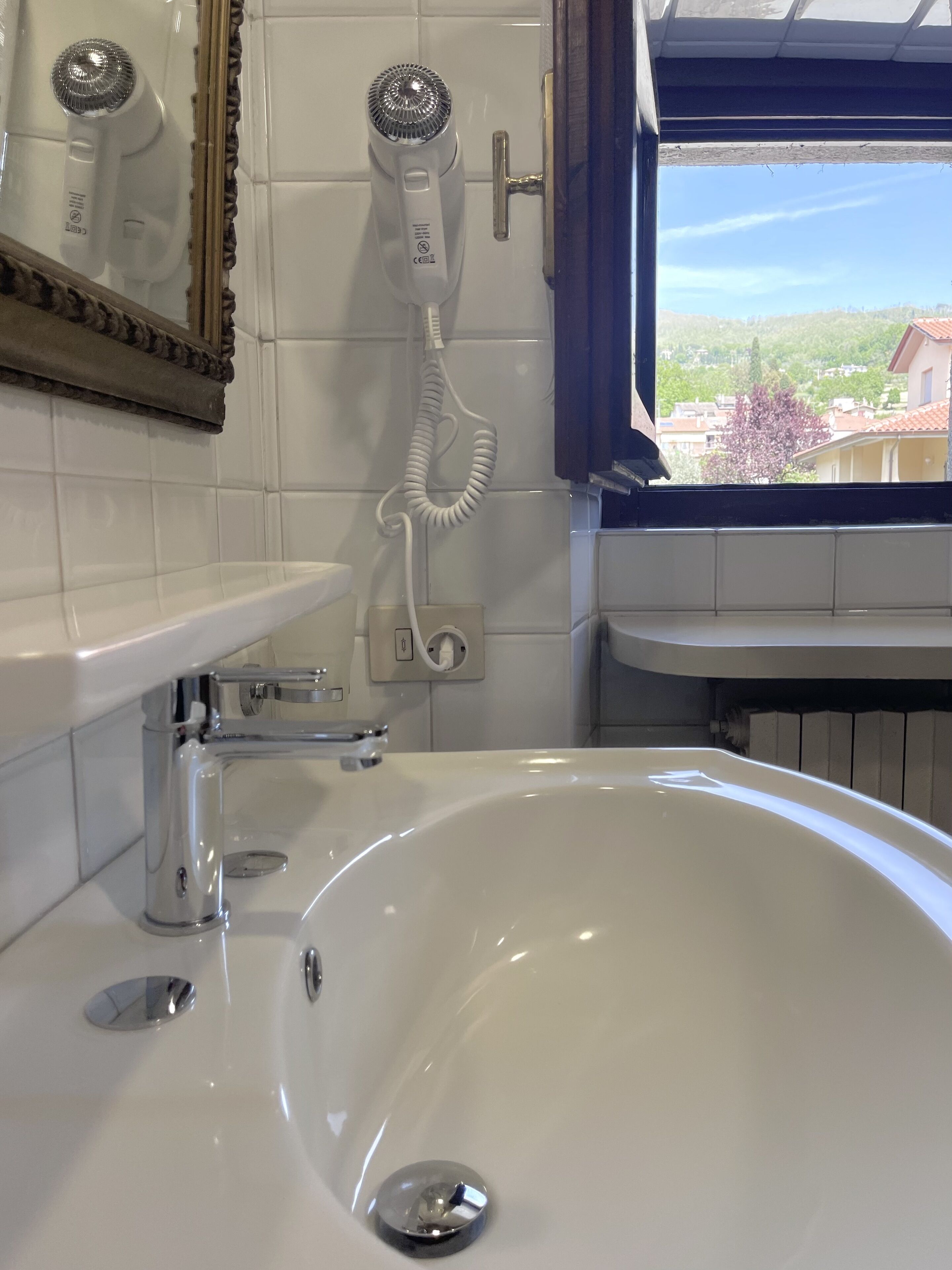 Casa de banho com lavatório branco, secador de cabelo e espelho.