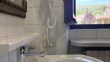 Casa de banho com lavatório branco, secador de cabelo e espelho.