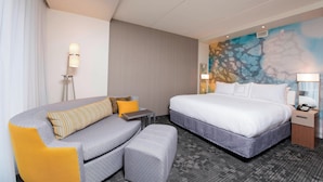 Quarto de hotel com uma cama, um sofá, uma mesinha e uma criadeira.