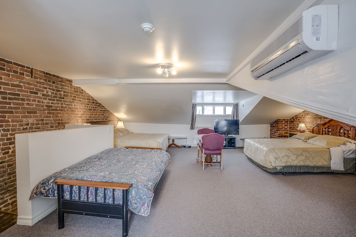 Quarto estilo loft com duas camas, uma escrivaninha, uma cadeira e uma televisão.