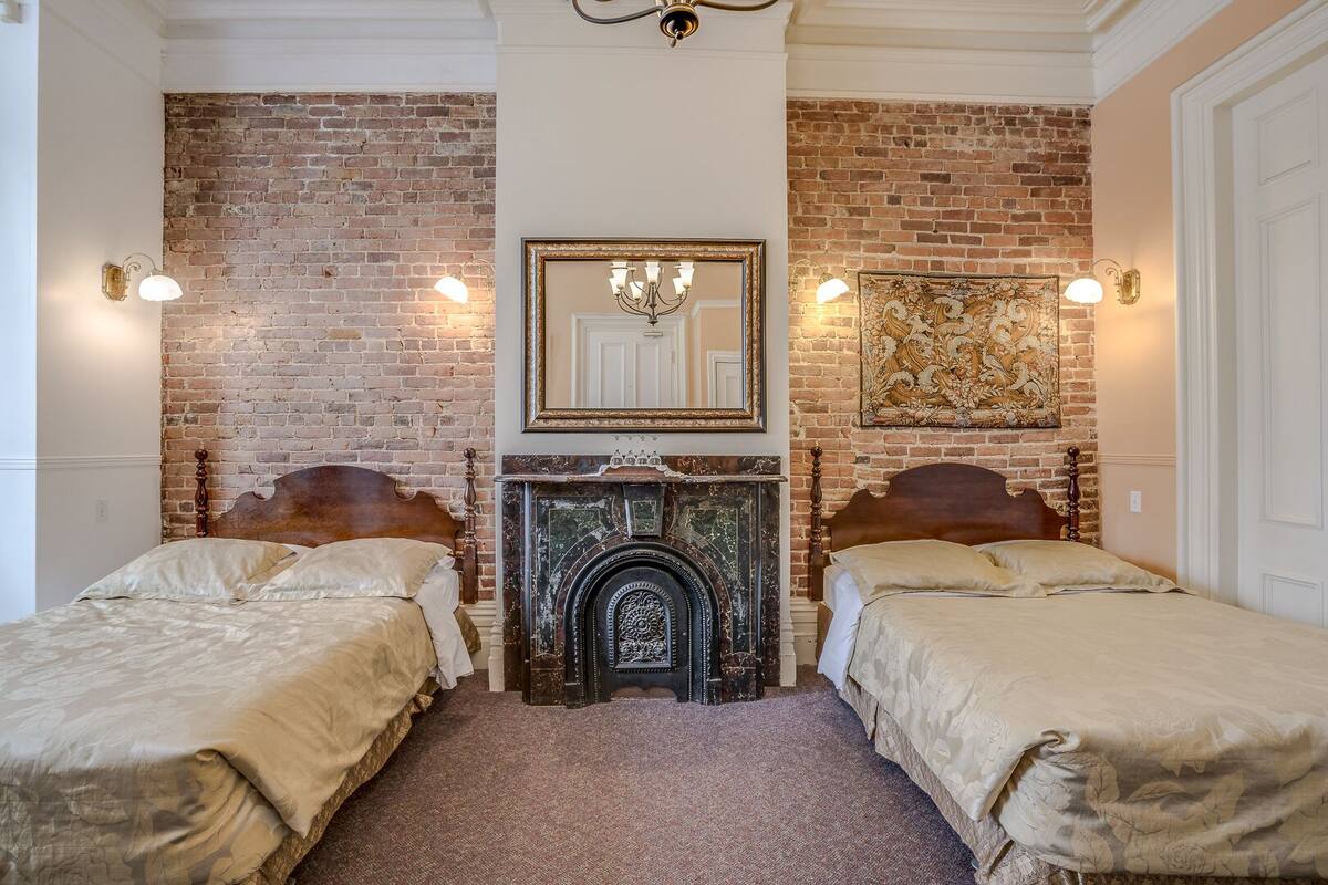Quarto com duas camas, lareira, espelho e paredes de tijolo.