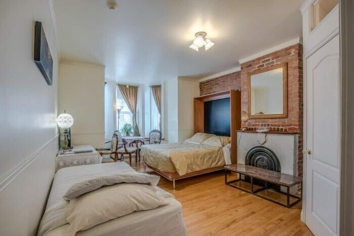Quarto com duas camas, lareira de tijolos, um espelho e um banco de madeira.
