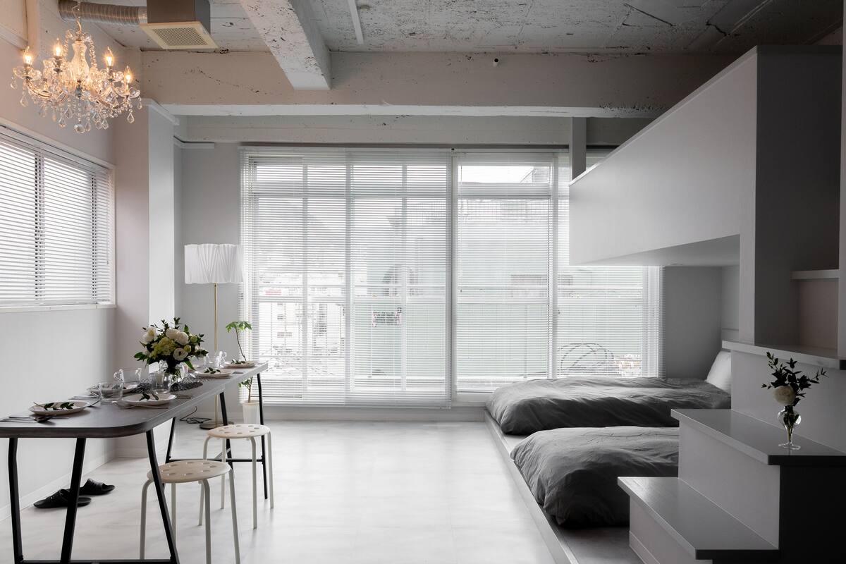 Quarto moderno com beliche, área de refeições com mesa e cadeiras, e janelas amplas com persianas.