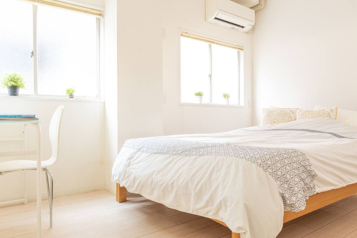 Quarto com cama, escrivaninha e duas janelas.