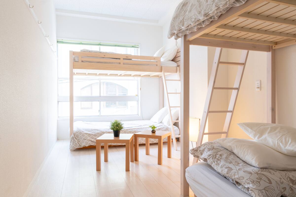 Quarto com beliche, janela, uma mesinha com uma planta e uma escada.