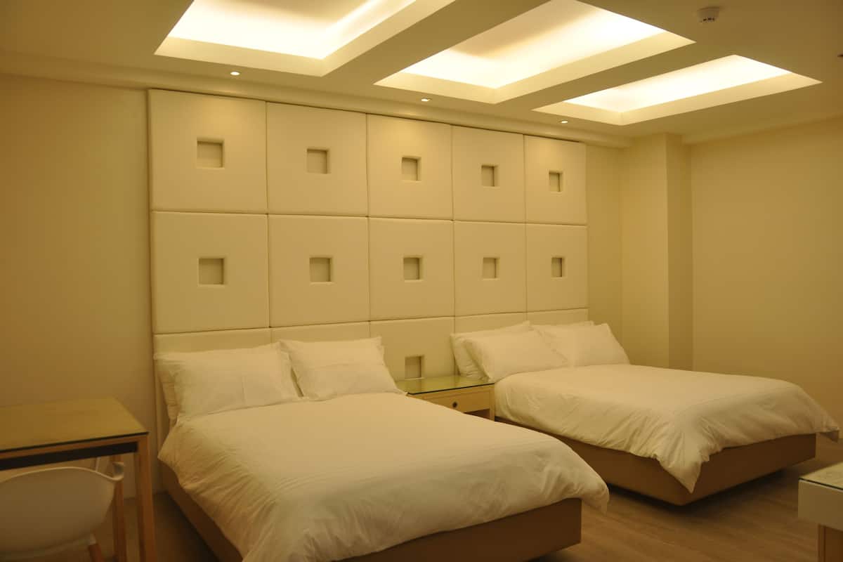 Quarto de hotel com duas camas, uma escrivaninha e uma cadeira.