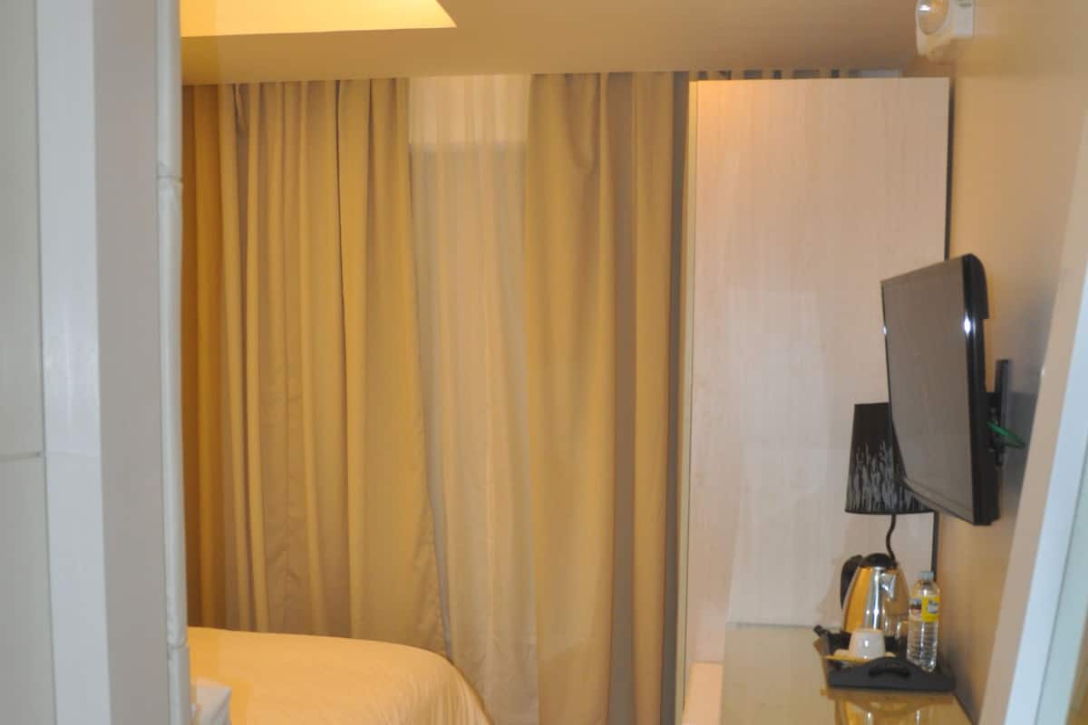 Quarto de hotel com cama, escrivaninha, televisão de tela plana e abajur.