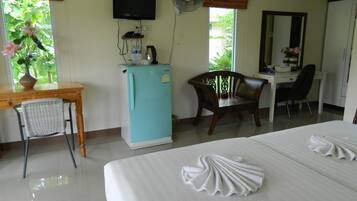 Quarto de hotel com cama, escrivaninha com cadeira, mini-frigorífico, televisão, ventoinha e janela com vista para área verde.