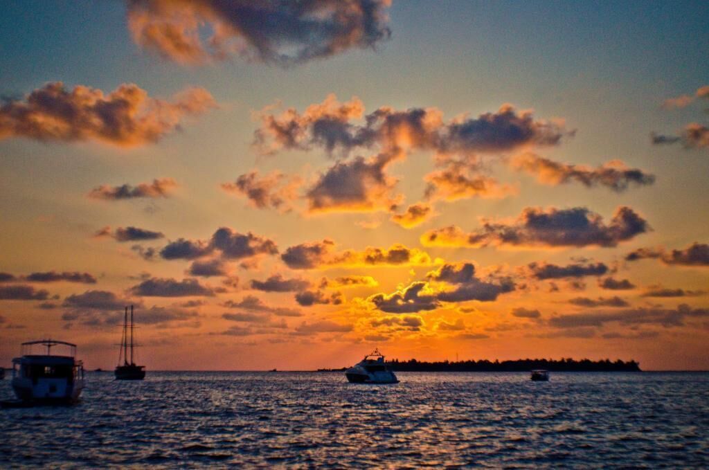 Um pôr do sol sobre um mar calmo, com vários barcos.