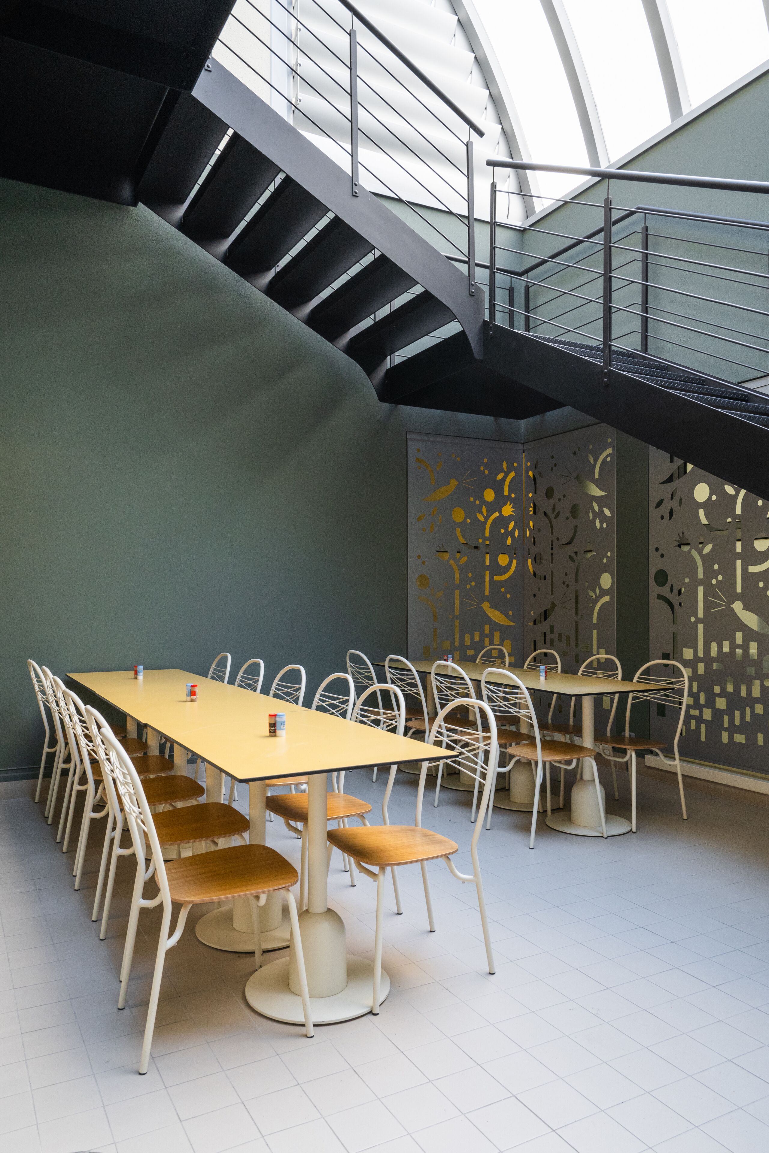 Uma área de refeições com mesas e cadeiras, uma escada e um painel decorativo.