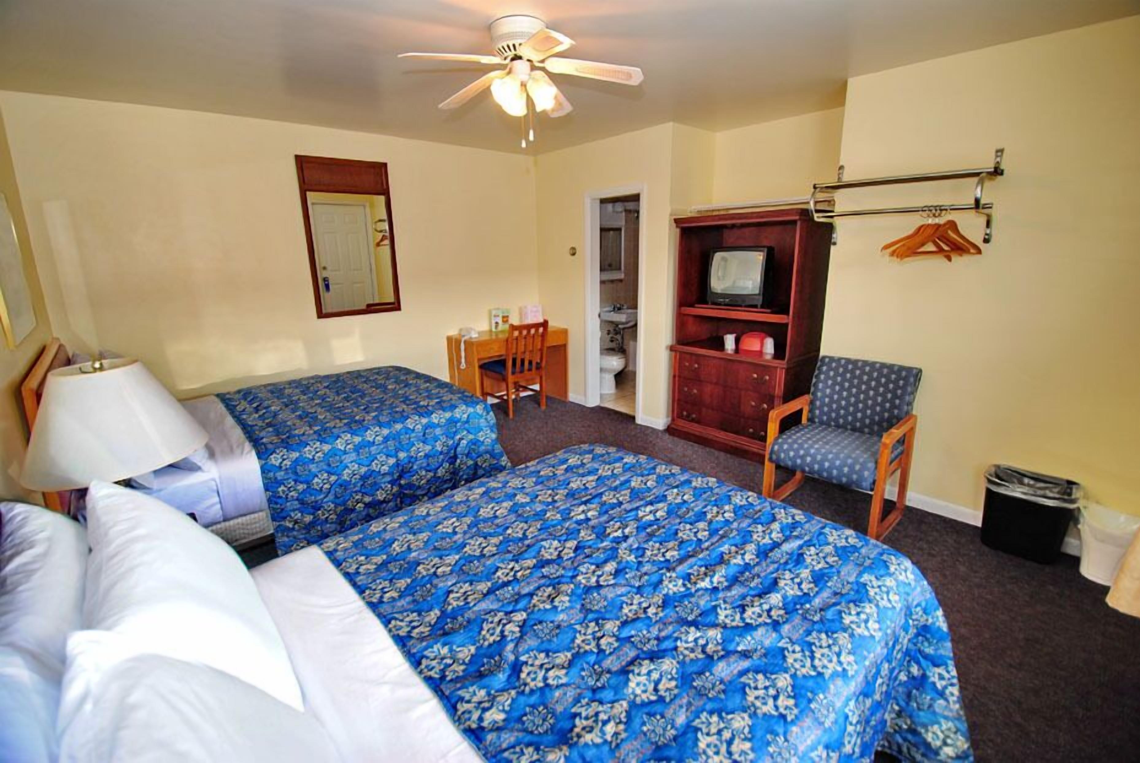 Quarto de hotel com duas camas, uma escrivaninha, uma cadeira, televisão e ventoinha no teto.