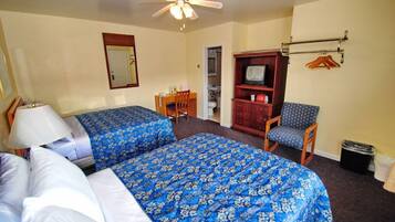 Quarto de hotel com duas camas, uma escrivaninha, uma cadeira, televisão e ventoinha no teto.