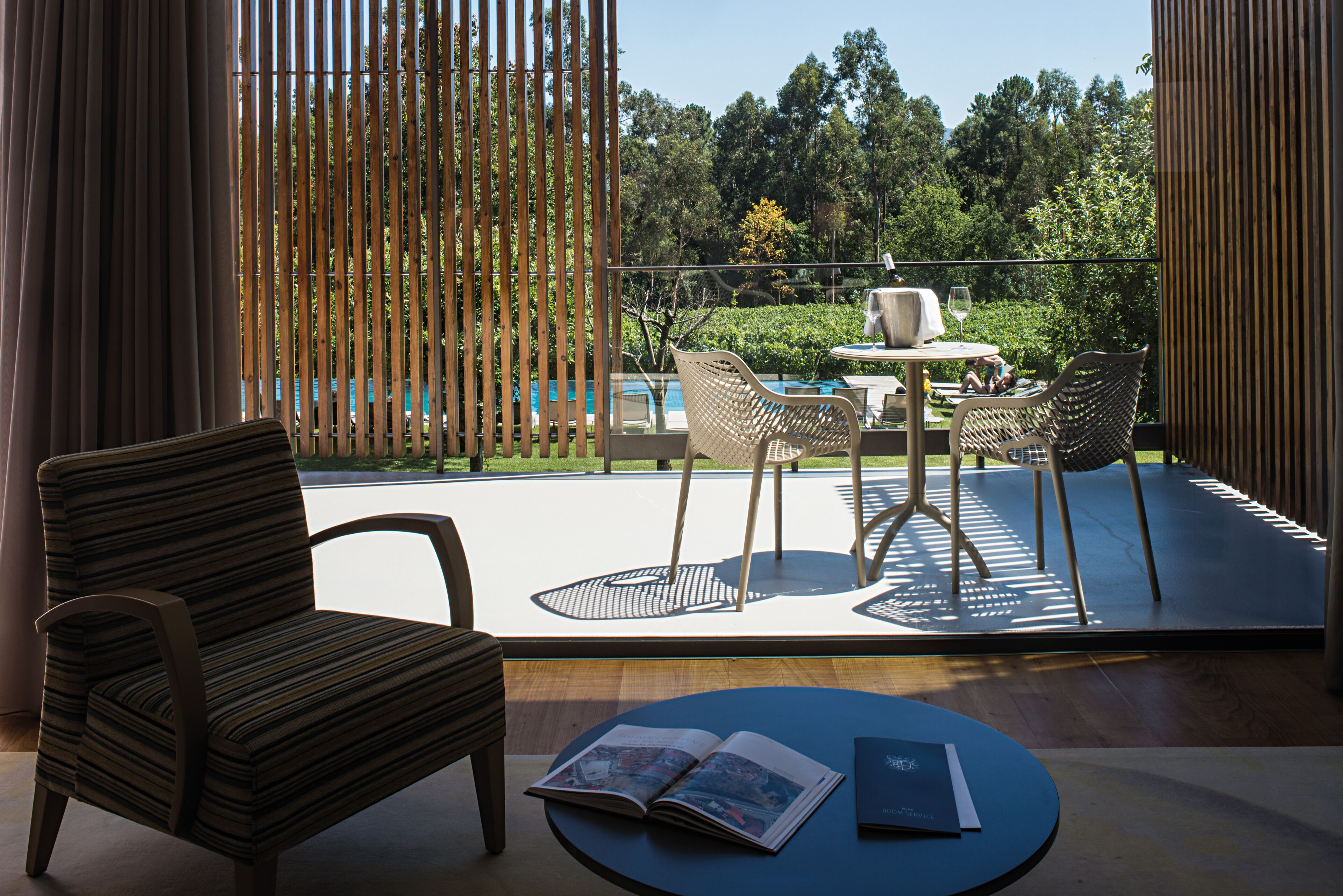 Uma área de estar moderna ao ar livre, vista para a piscina, com uma mesa redonda, duas cadeiras e um livro sobre a mesa.
